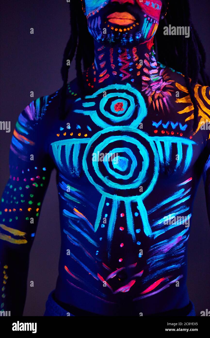 portrait of muscular young man in bright blacklight bodyart glowing in ...