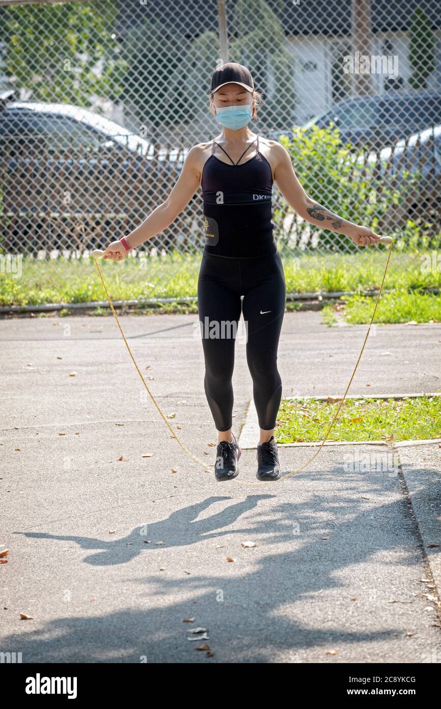 A fit Asian American young lady wearing a mask jumps rope as part of a ...