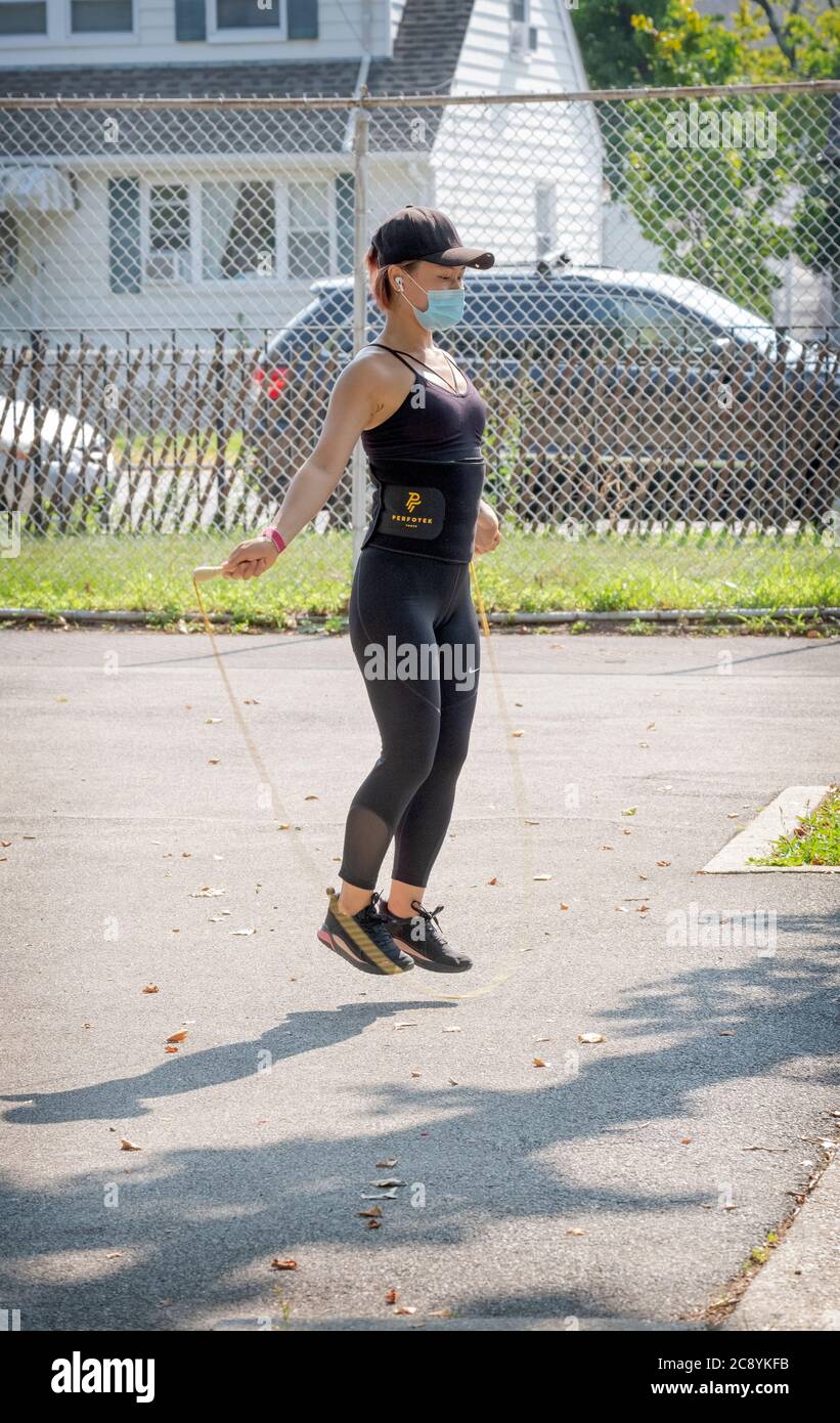 A fit Asian American young lady wearing a mask jumps rope as part of a ...