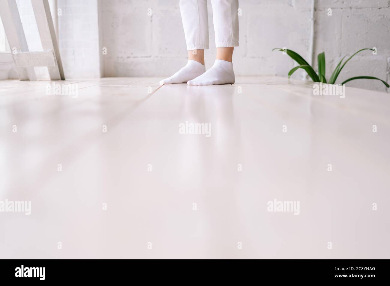 Close-up of feet of woman in white socks standing near big window on ...