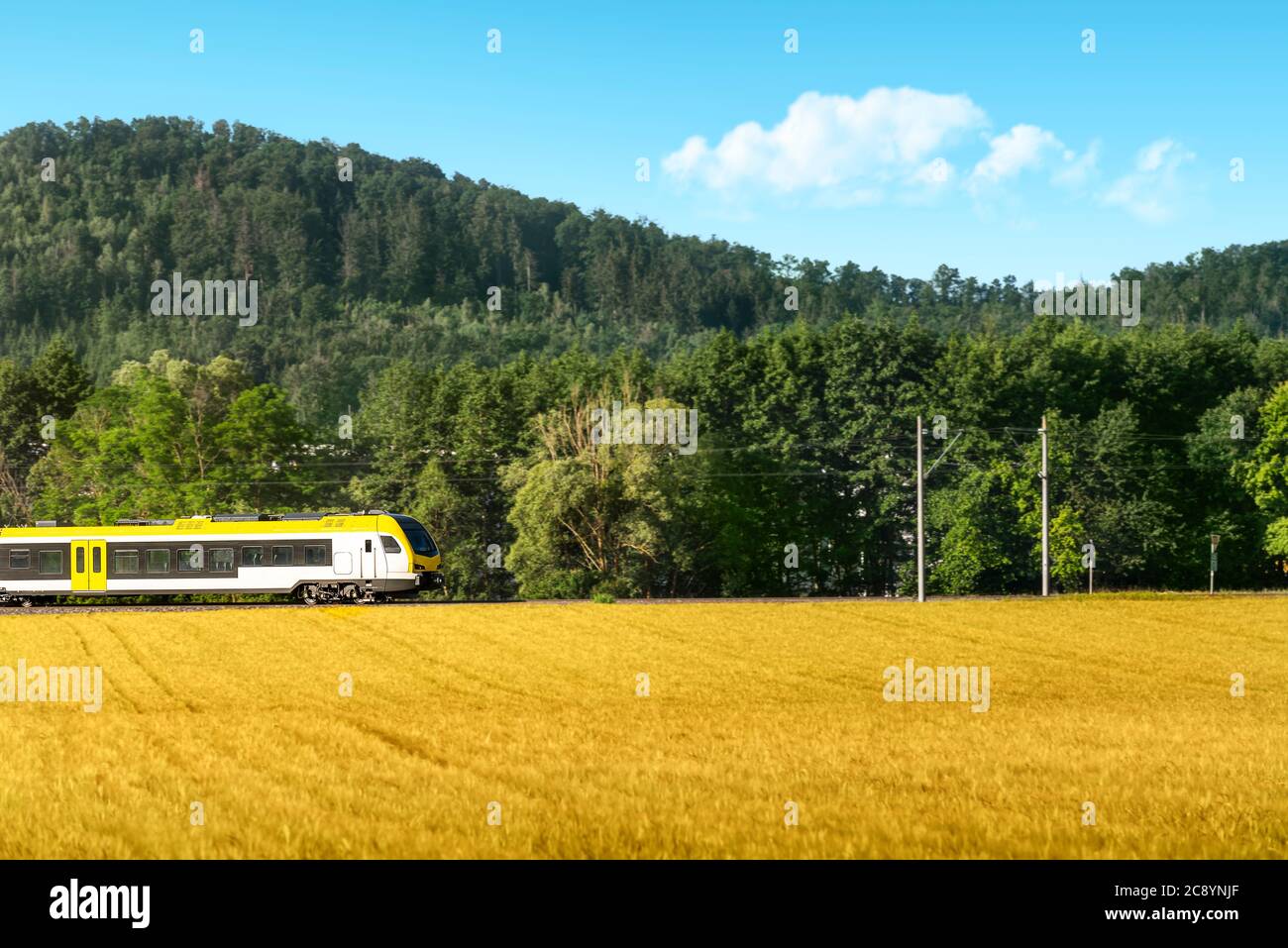 Electric train traveling through agricultural fields and forest, at ...