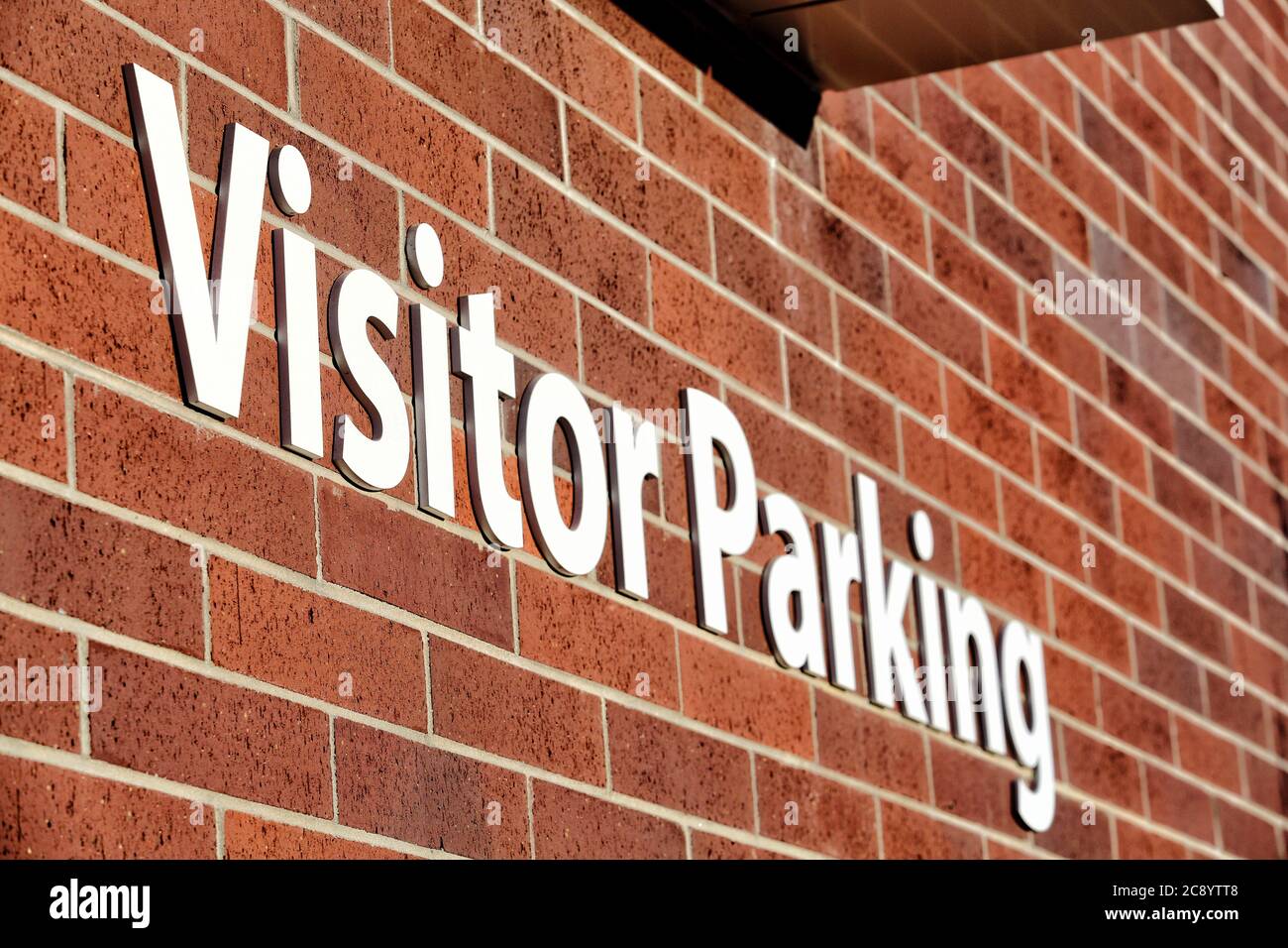 A white visitor parking sign in block letters, on a red brick wall ...