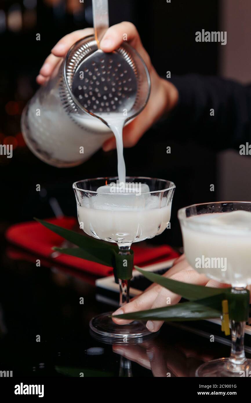 hands of a bartender holding a shaker pouring a drink into a glass ...