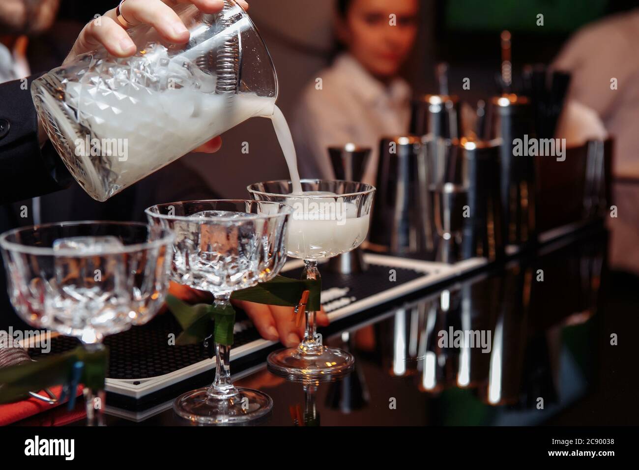 hands of a bartender holding a shaker pouring a drink into a glass ...