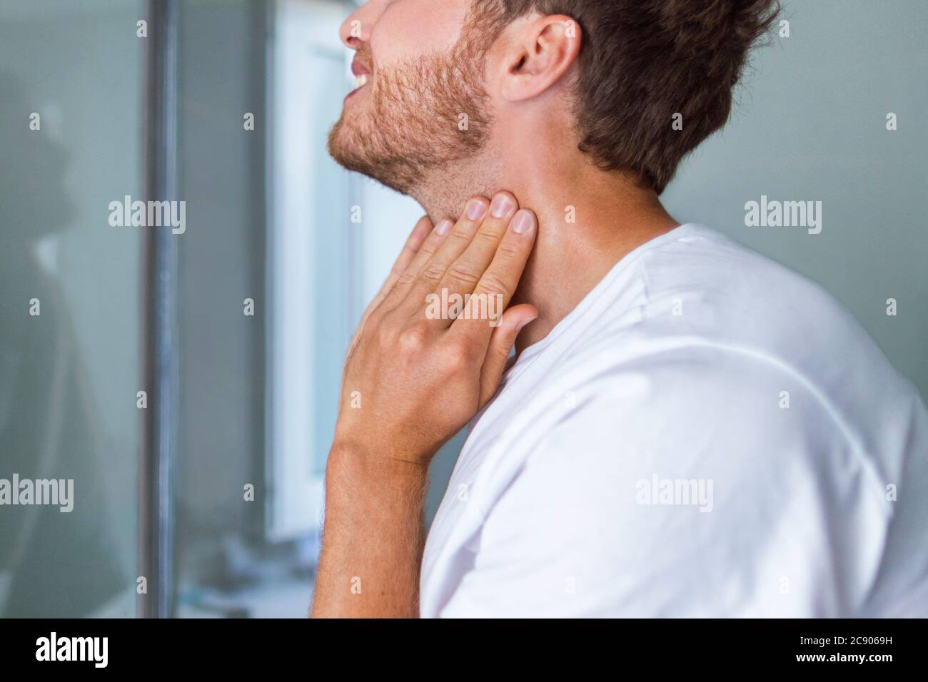 Thyroid self-exam checkup. Young man touching his neck at home bathroom ...