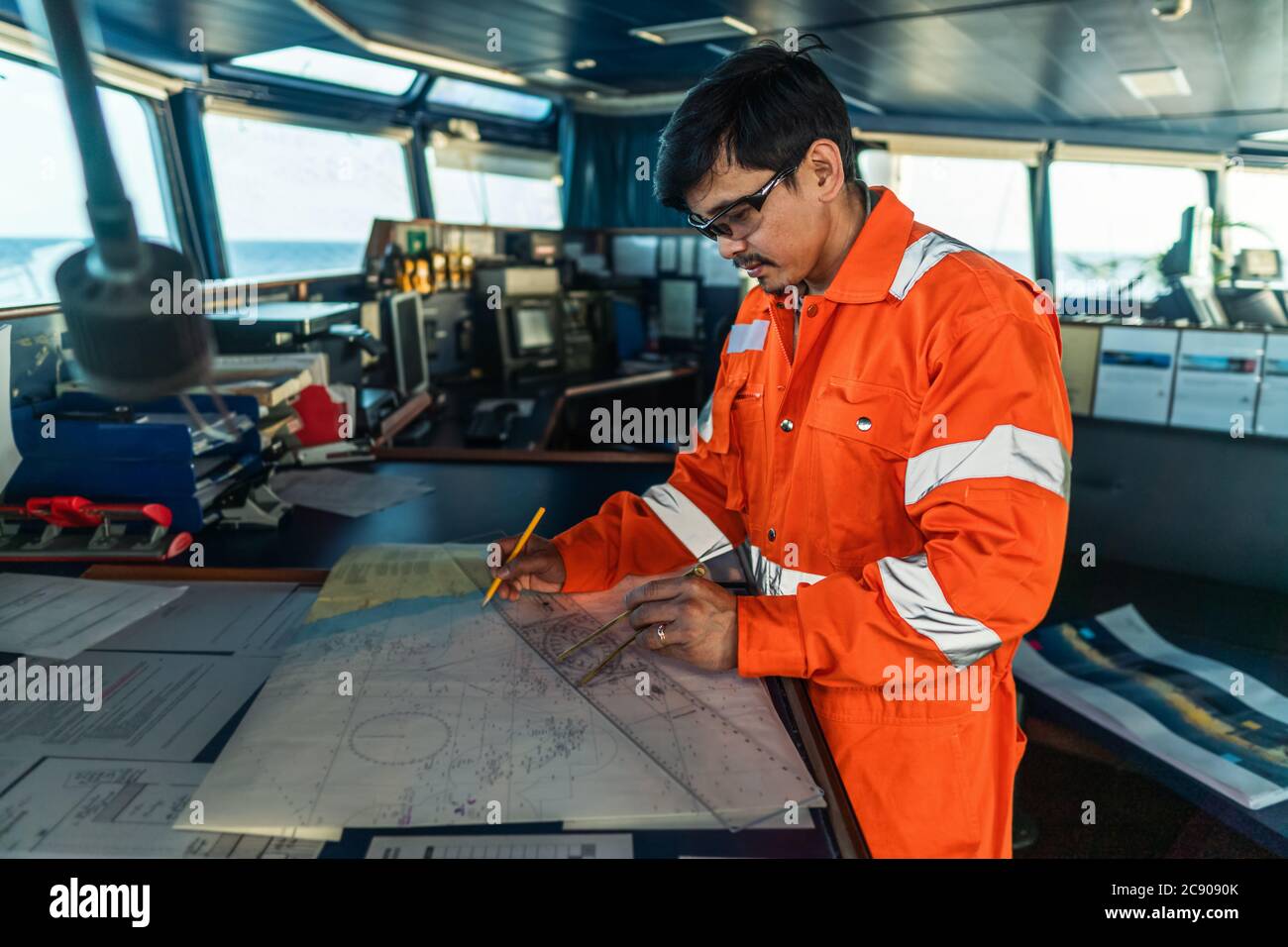 Filipino deck Officer on bridge of vessel or ship. He is plotting ...