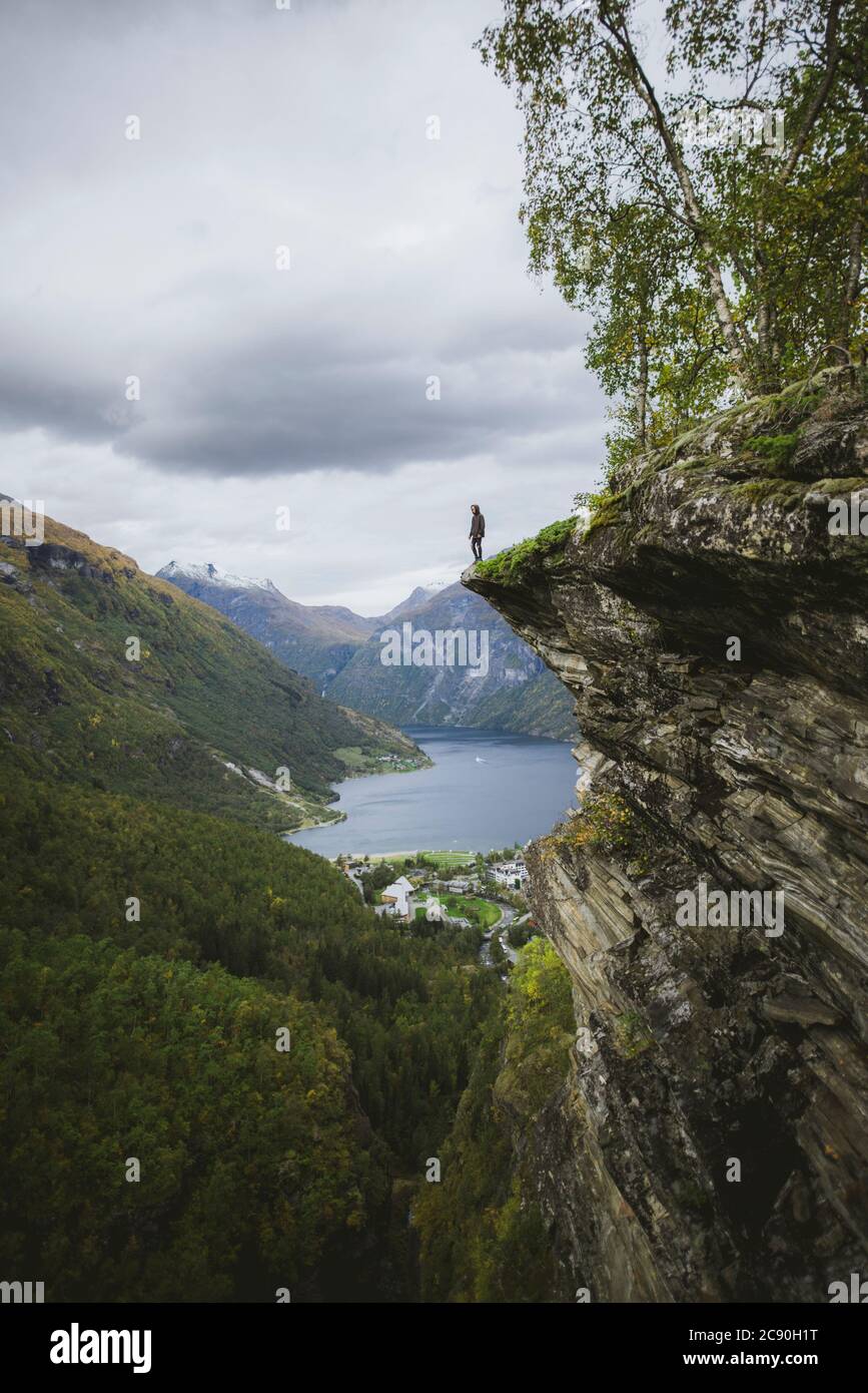 Norway, Geiranger, Man standing on edge of steep cliff above ...