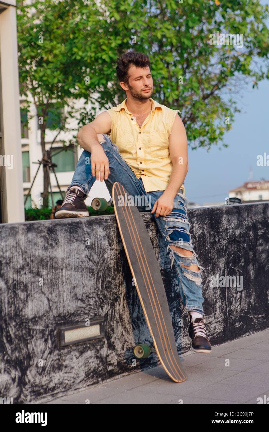 Young man sitting with longboard on the street Stock Photo - Alamy
