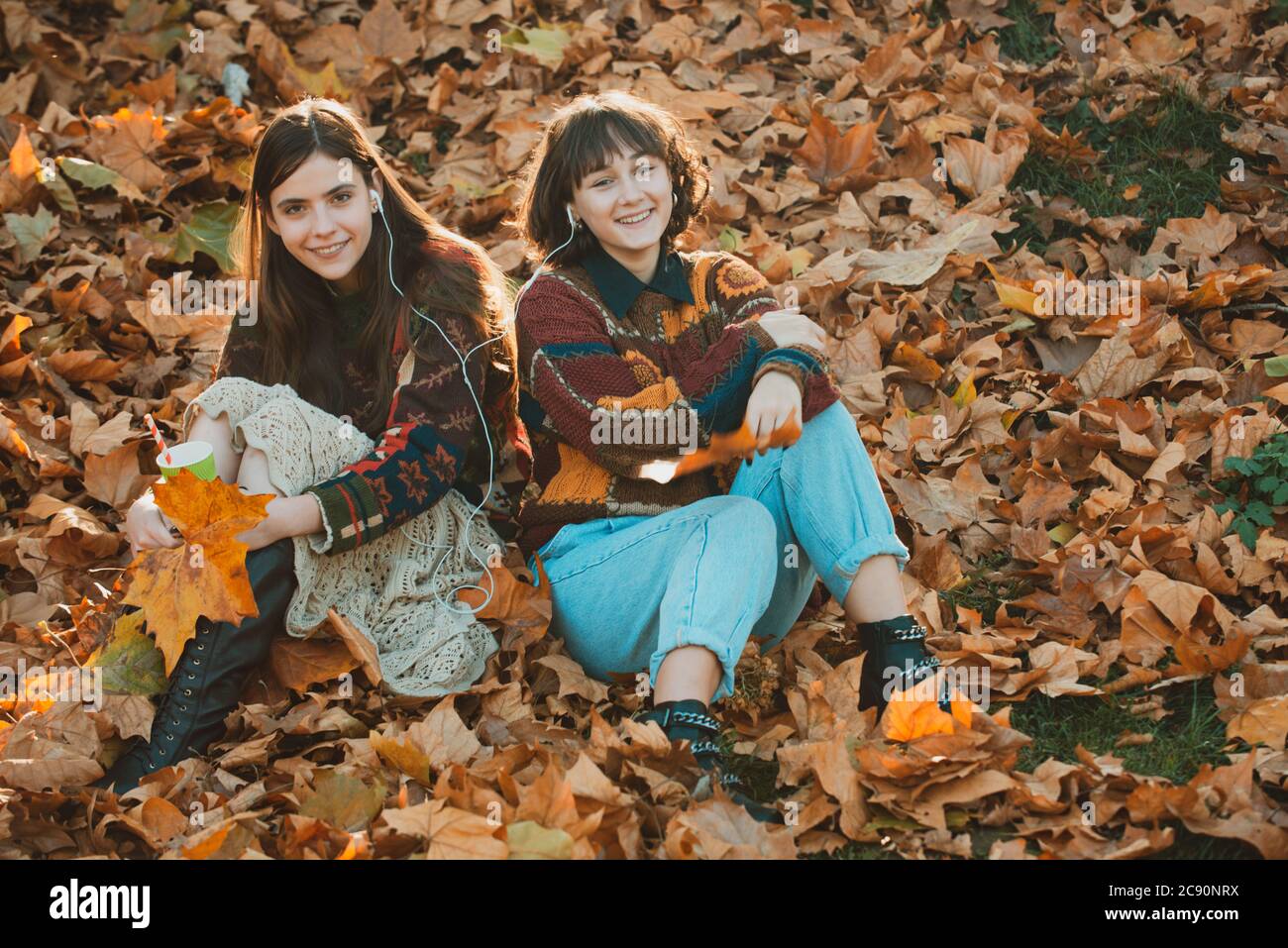Two girls smiling in autumn park. Cute young students sit in the autumn ...