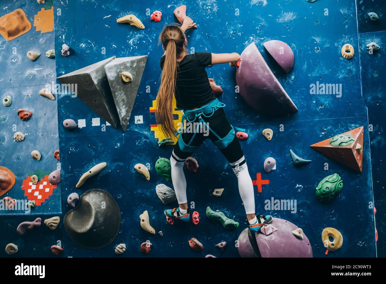 Young woman climbing a tall, indoor, man-made rock climbing wall Stock ...