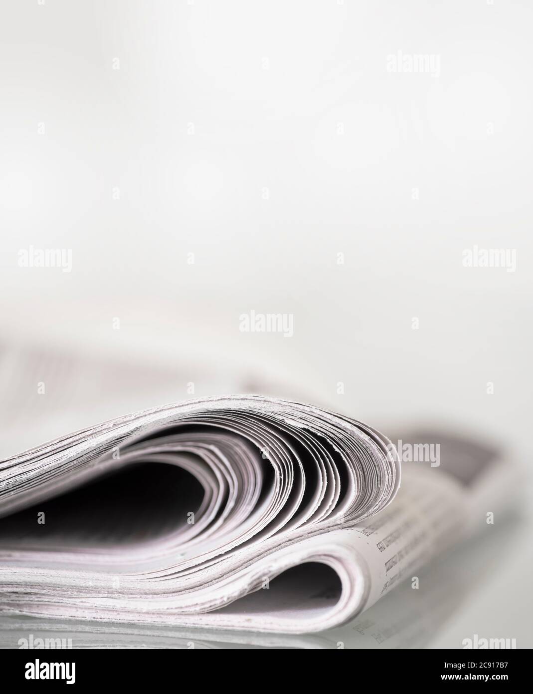 Folded newspaper mirrored on glass table against plain light background ...