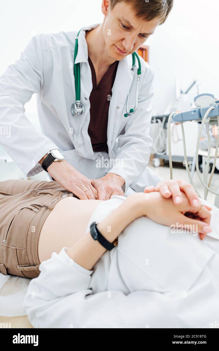 Doctor pressing his fingers against stomach of a young female patient ...