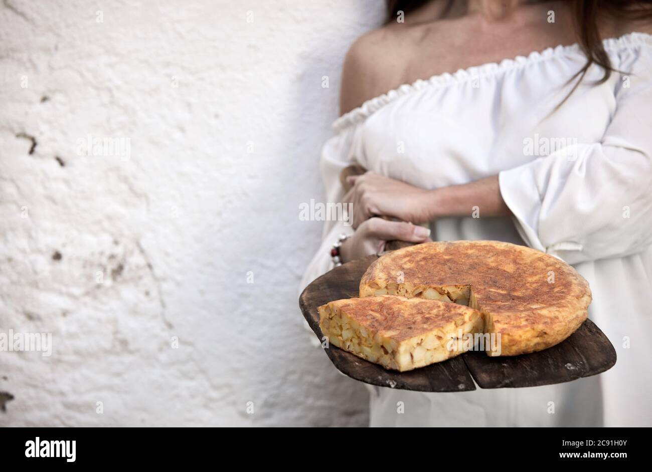 Woman holding a cut potato tortilla on a vintage wooden paddle outdoors ...