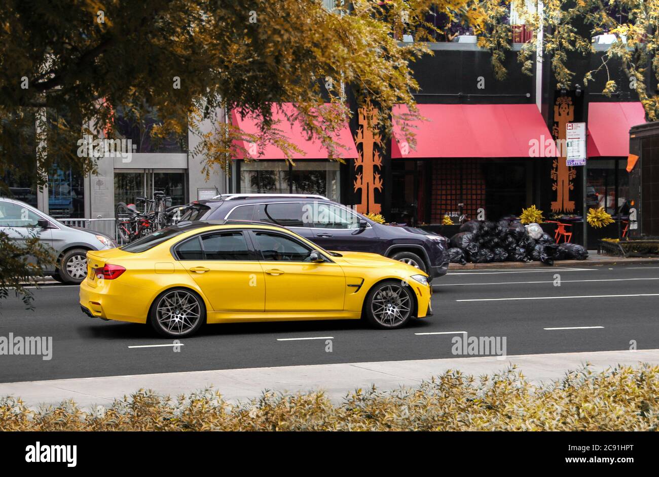 Yellow BMW M3 F80 performance saloon driven on a street in central New ...
