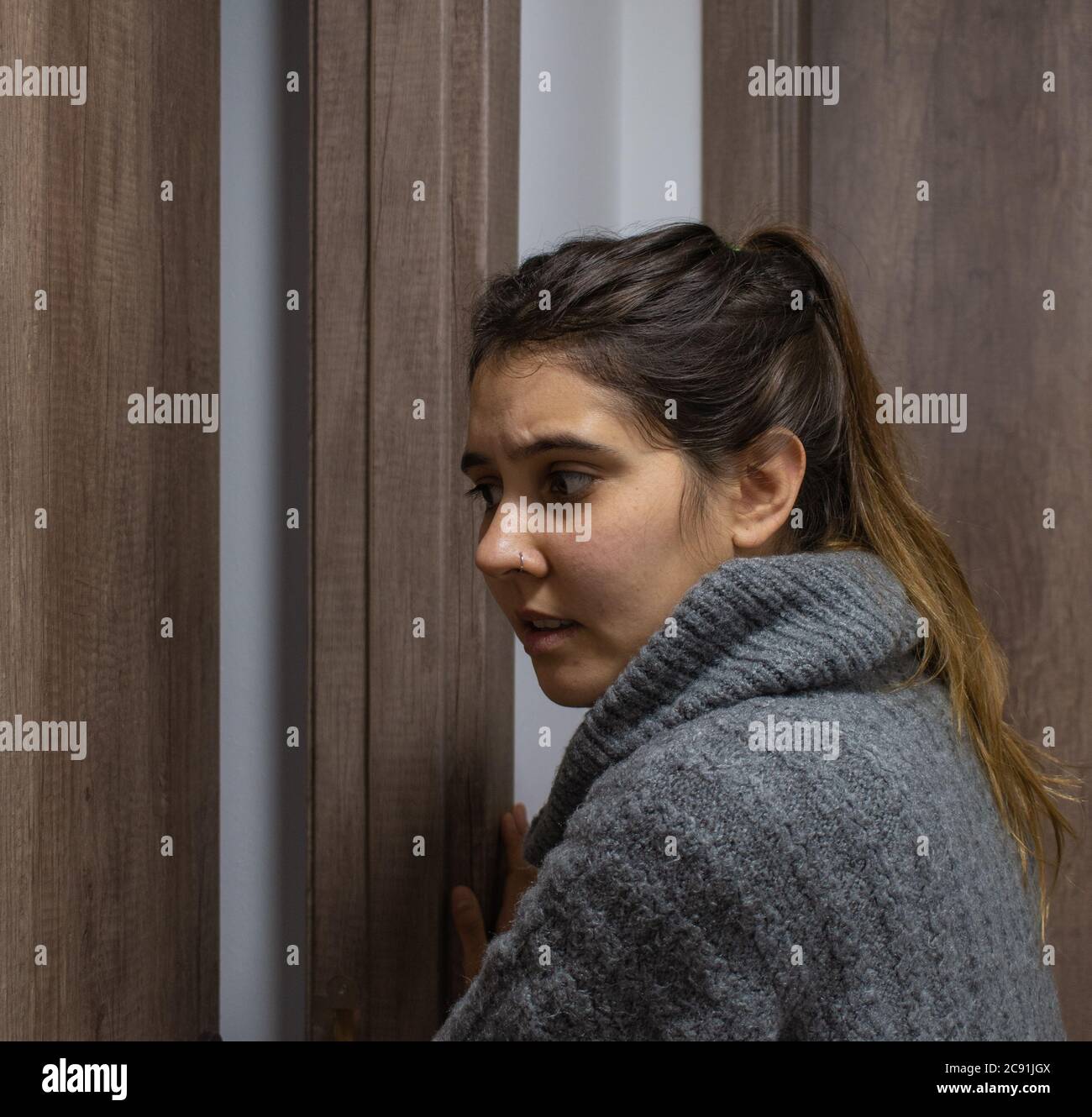 Concerned female eavesdropping outside the wooden door under the lights ...