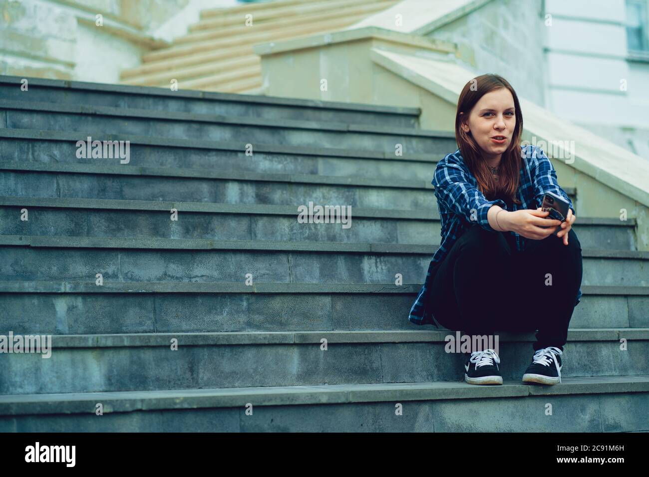 Young woman sitting on stairs of manor with smartphone in hands. Adult ...