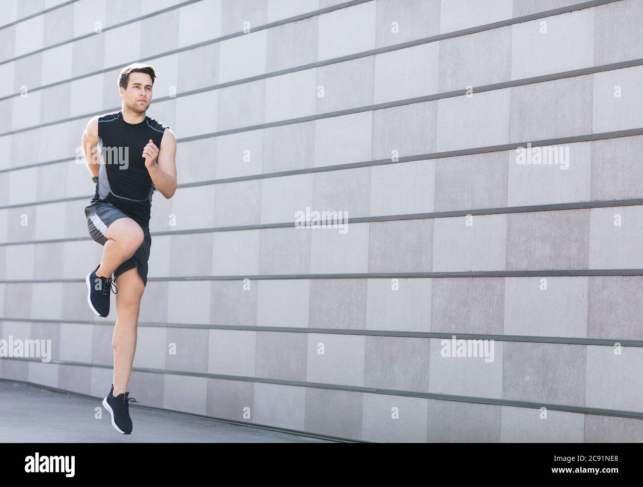 Jogging in street. Young man in sportswear and sneakers jumps and runs ...