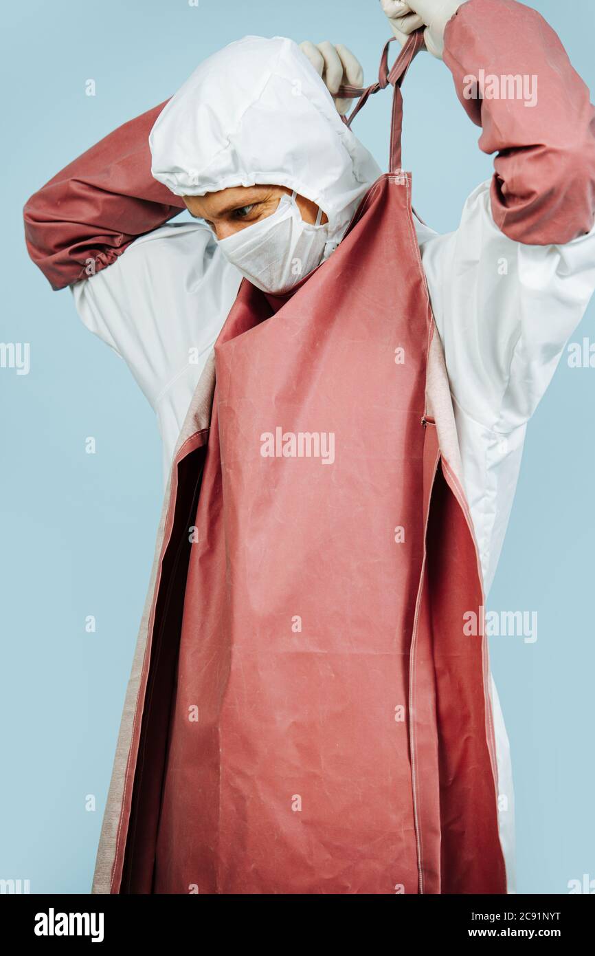 Doctor in a white costume covering all skin putting on surgeon apron ...