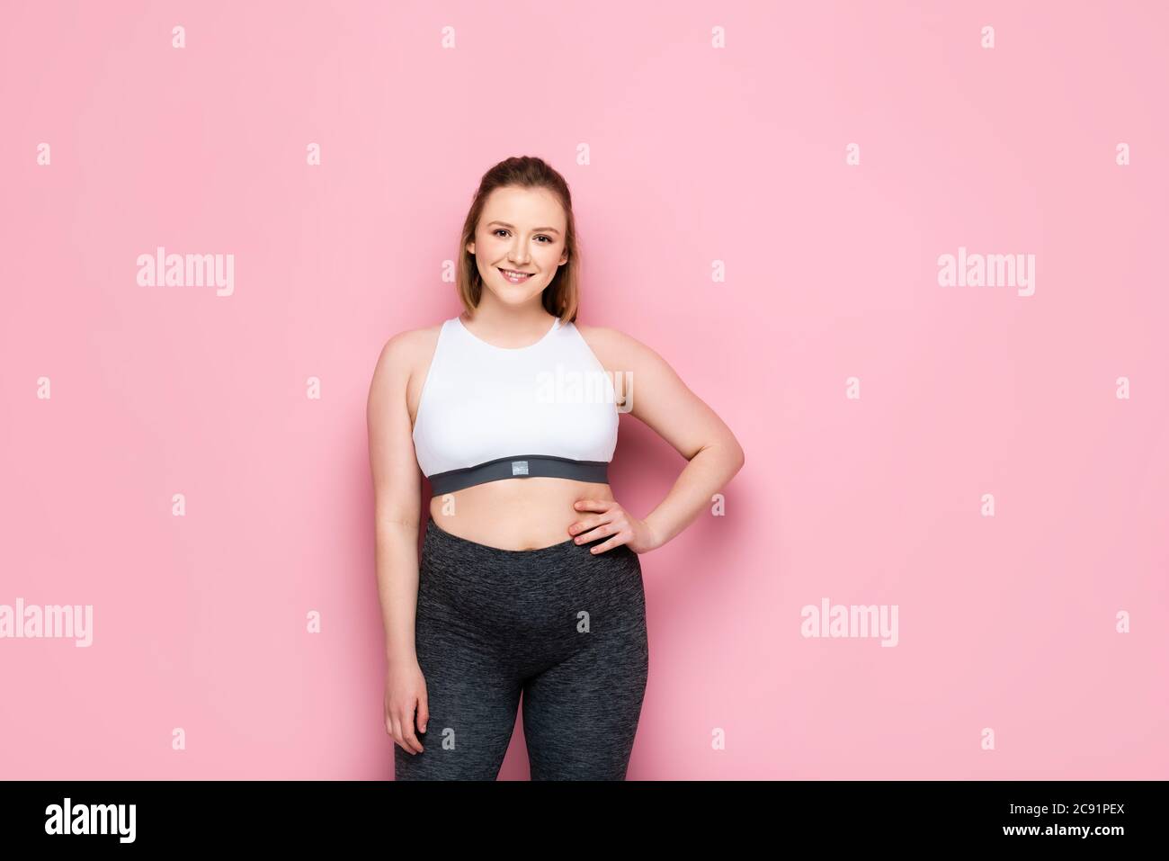 pretty overweight girl in sportswear holding hand on hip and smiling on ...