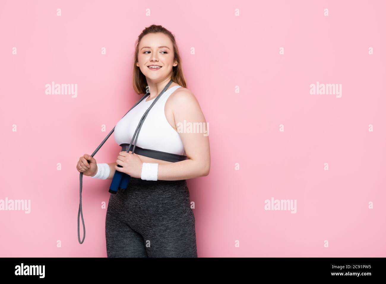 smiling overweight girl with jumping rope around neck looking away on ...