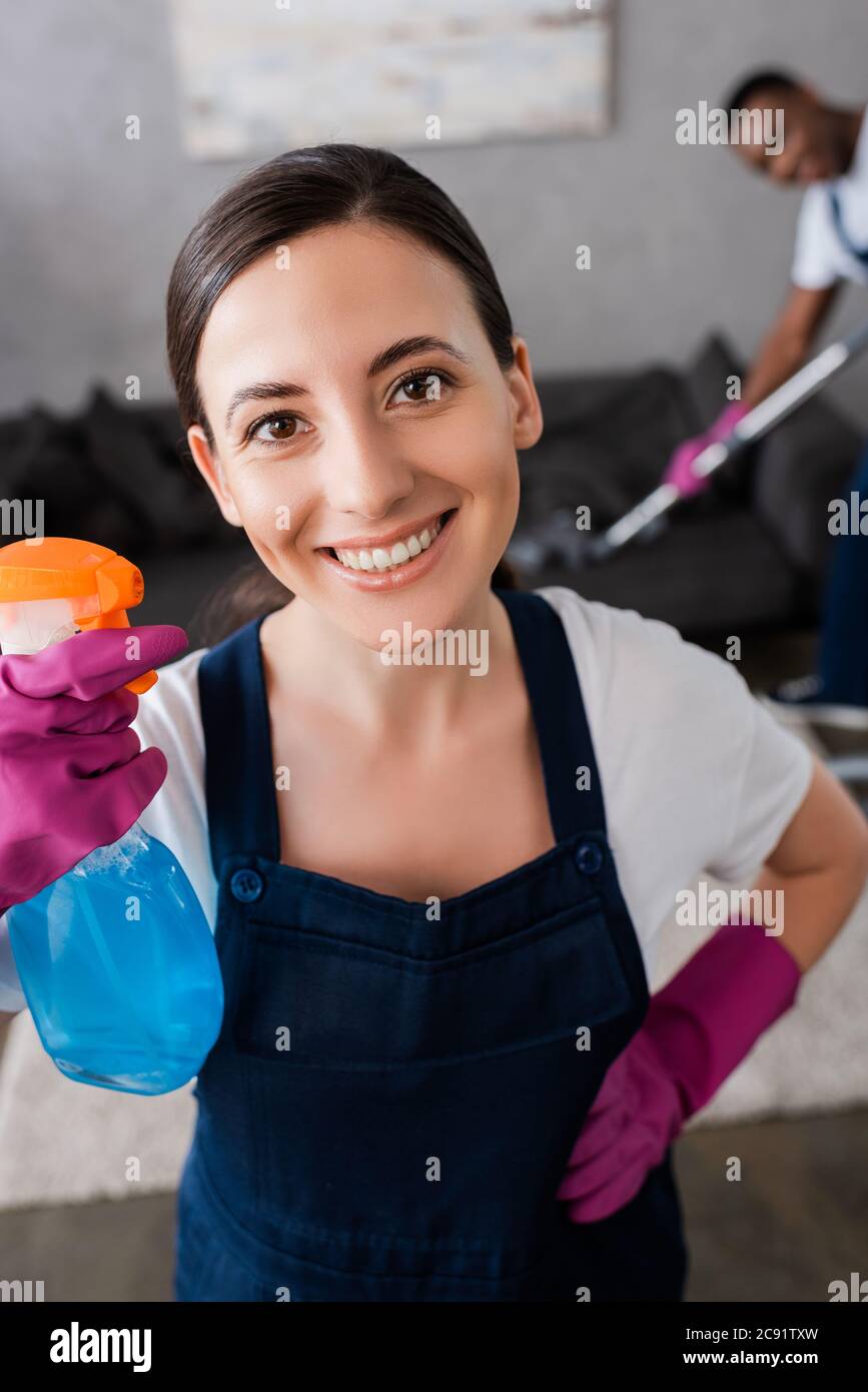 Selective focus of smiling cleaner holding detergent while working with ...