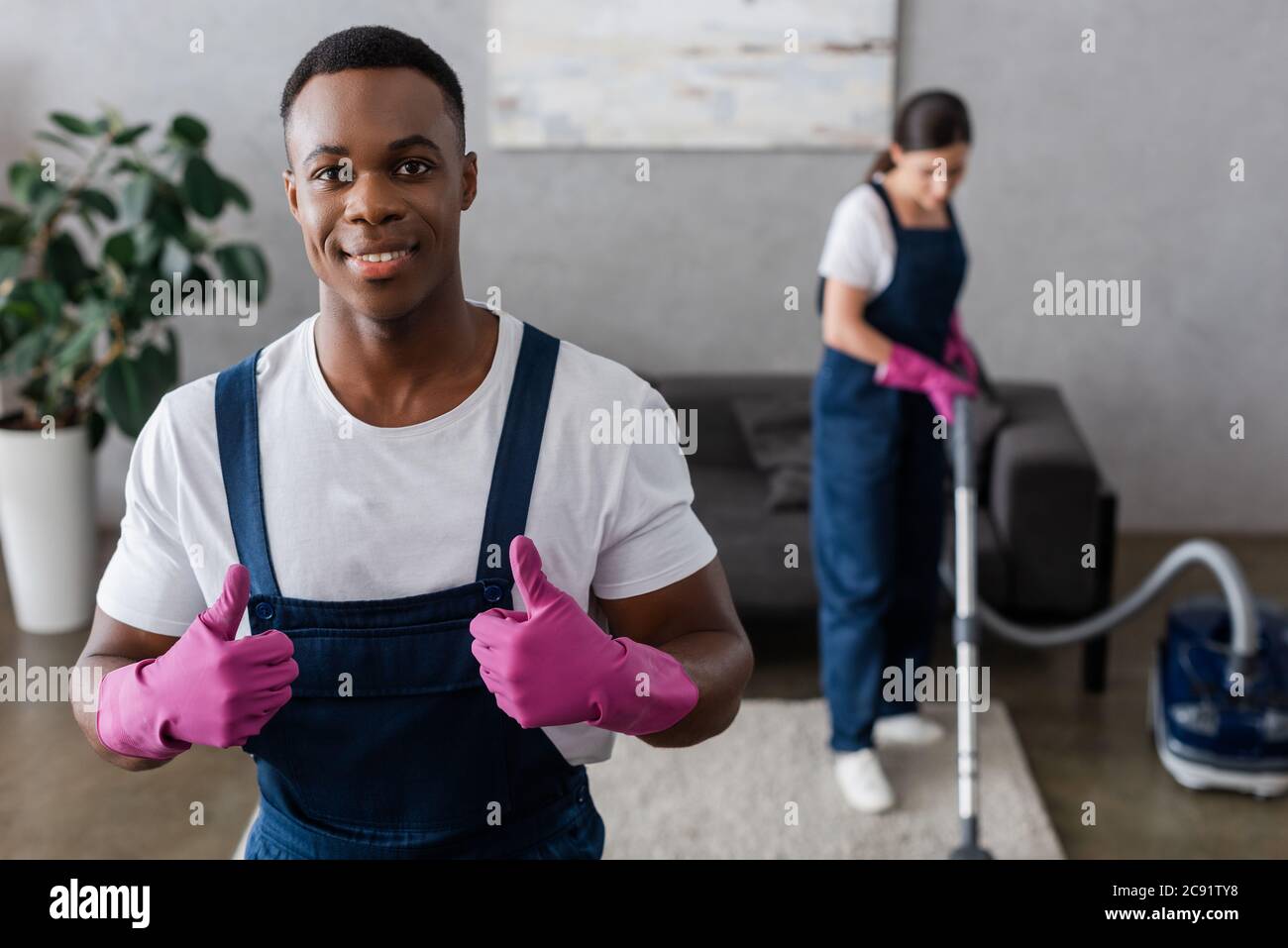 Selective focus of smiling african american cleaner showing thumbs up ...