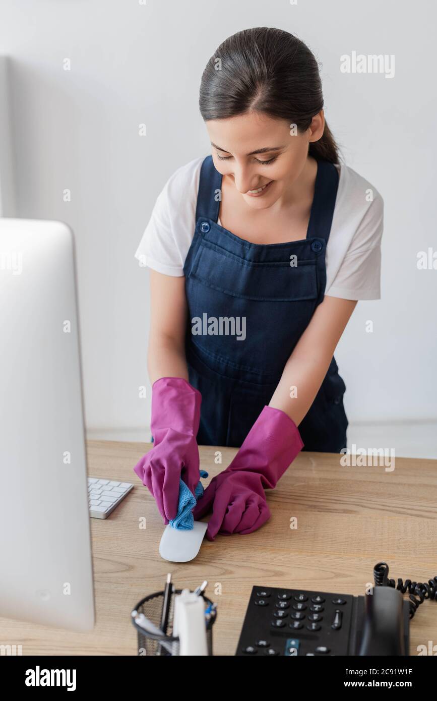 Selective focus of smiling cleaner holding rag while cleaning computer ...