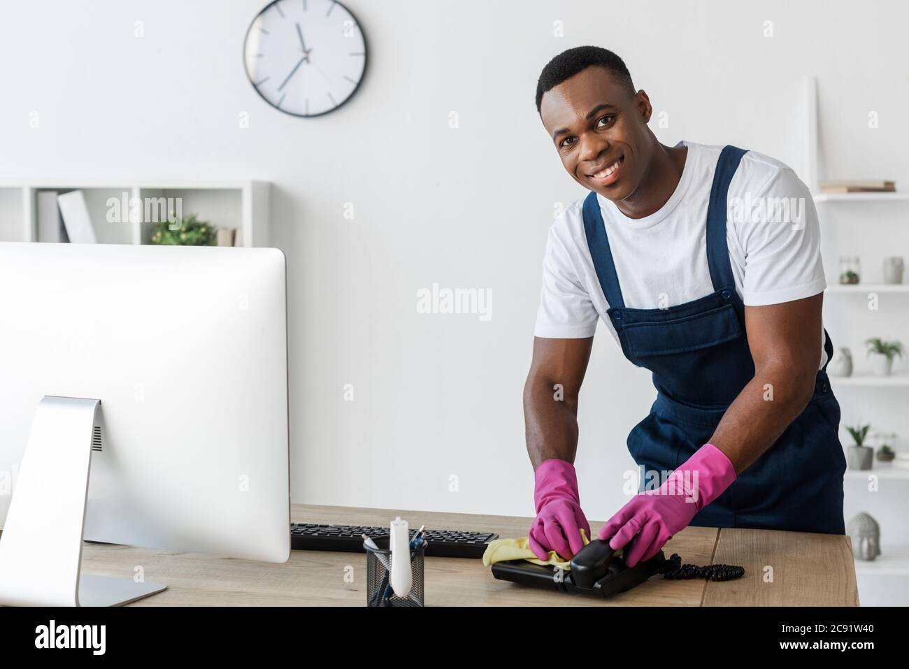 Selective focus of smiling african american cleaner cleaning telephone ...