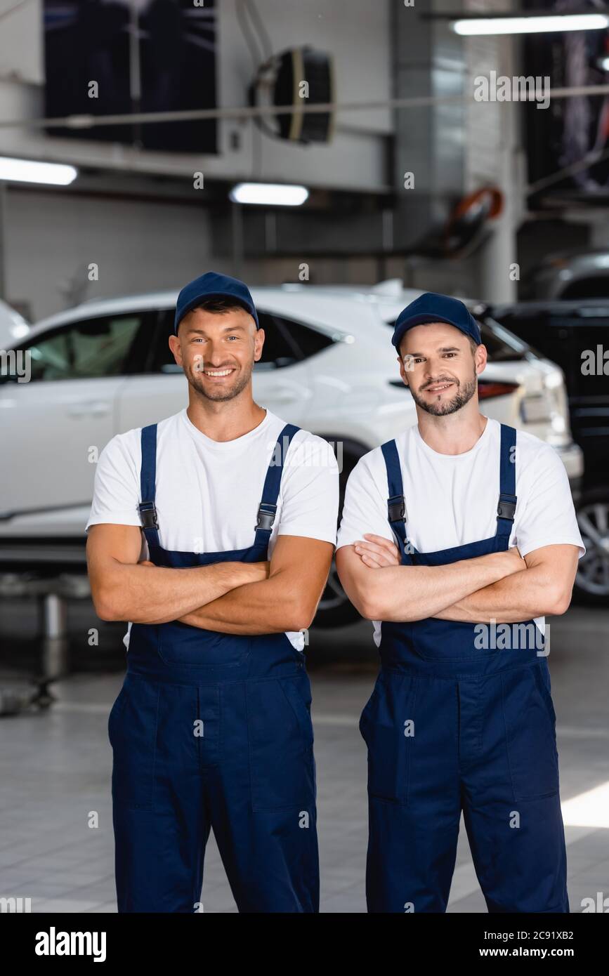 happy mechanics in uniform and caps standing with crossed arms in car ...