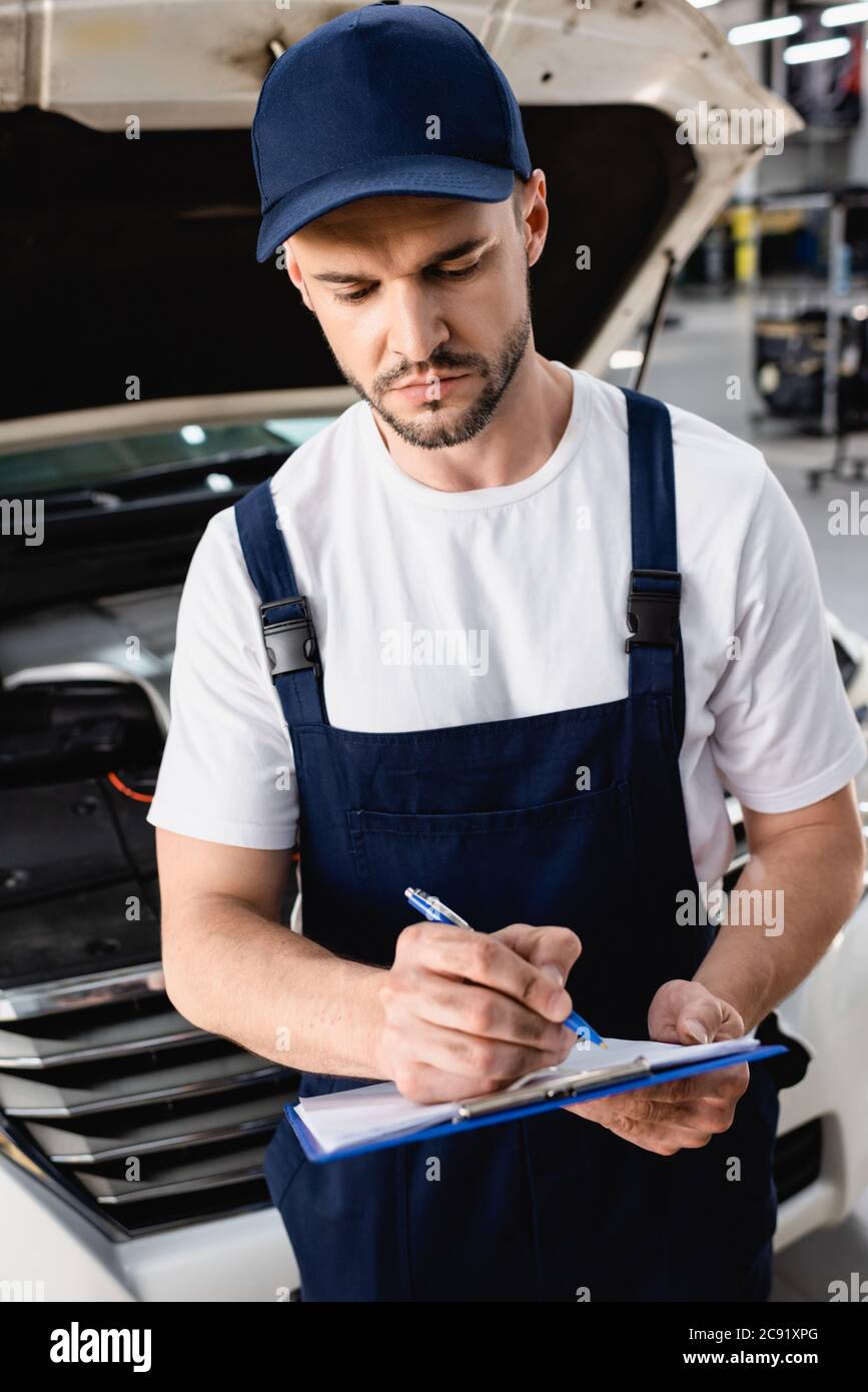 Auto mechanic writing on clipboard near open hood of car at service ...