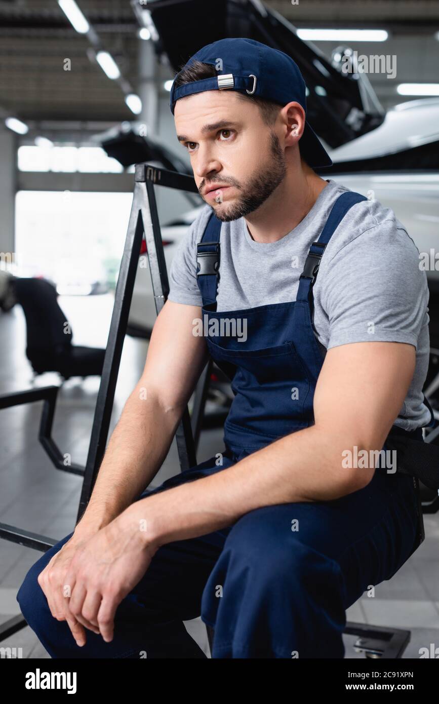 Tired auto mechanic sitting near cars at service station Stock Photo ...