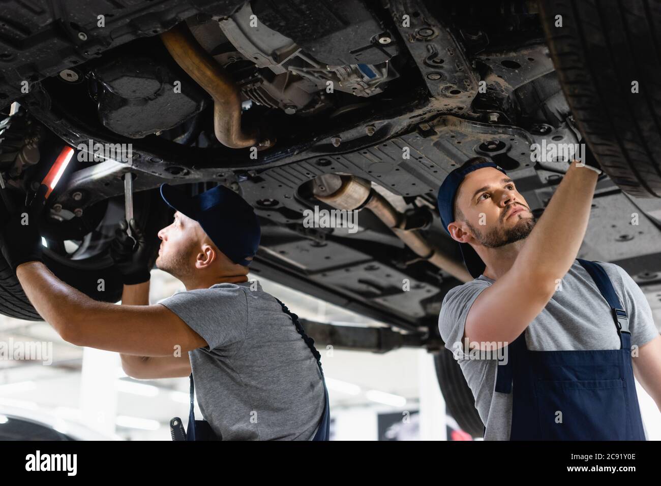 low angel view of handsome mechanics in caps fixing car in service ...
