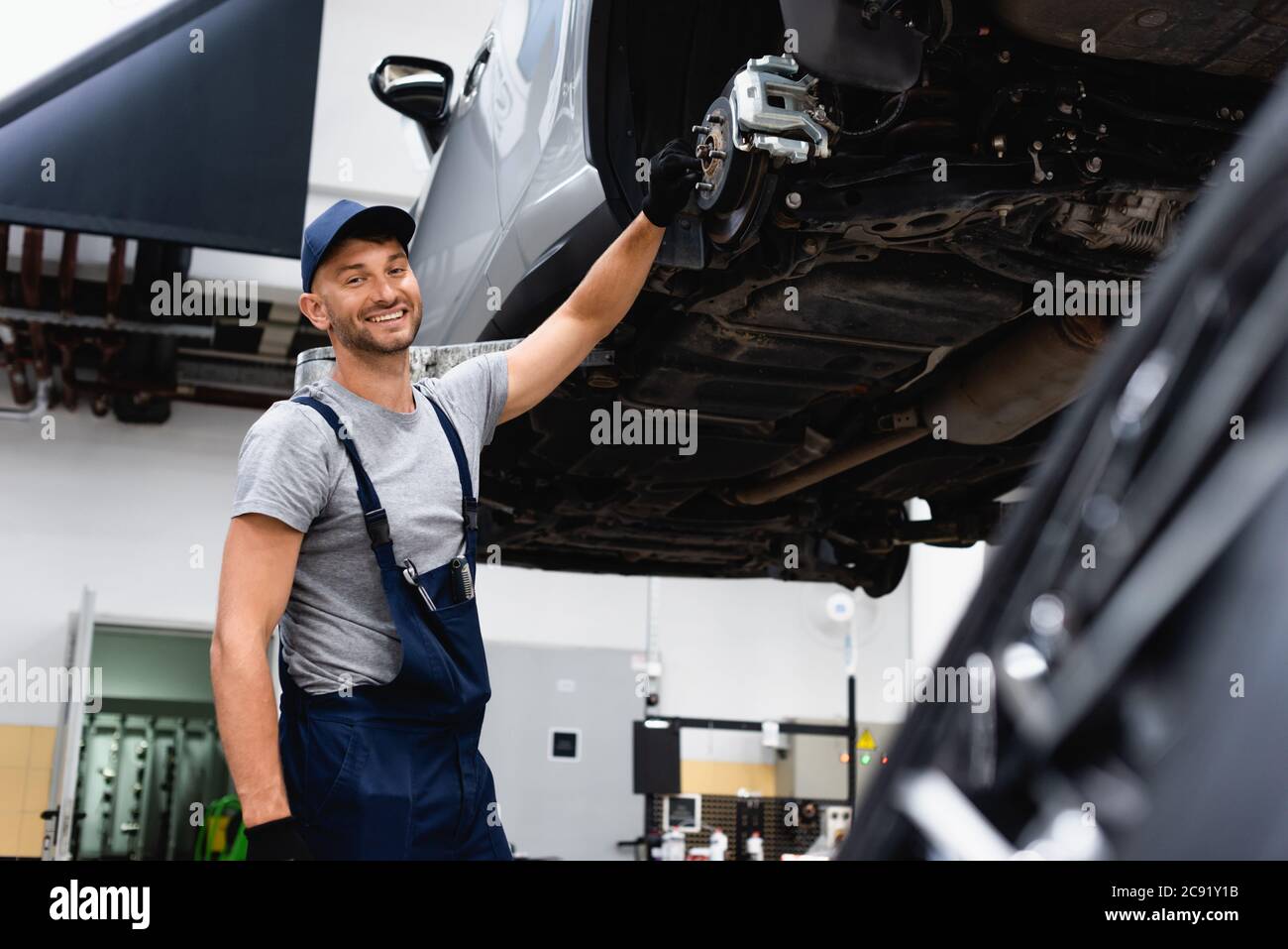 selective focus of happy mechanic in overalls standing near car Stock ...