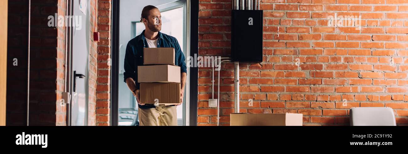 panoramic concept of handsome businessman holding carton boxes while ...