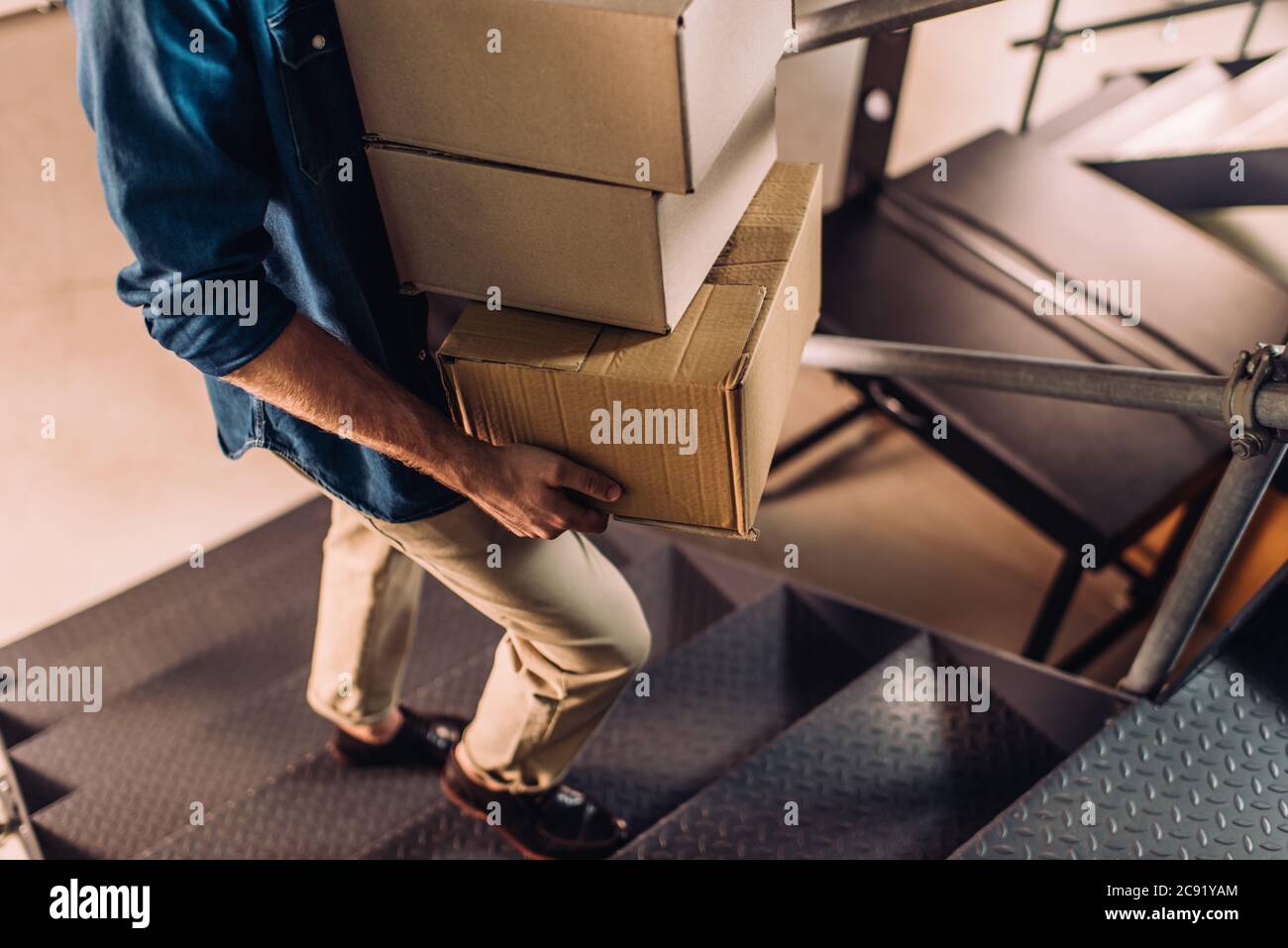 partial view of businessman holding carton boxes and walking on stairs ...