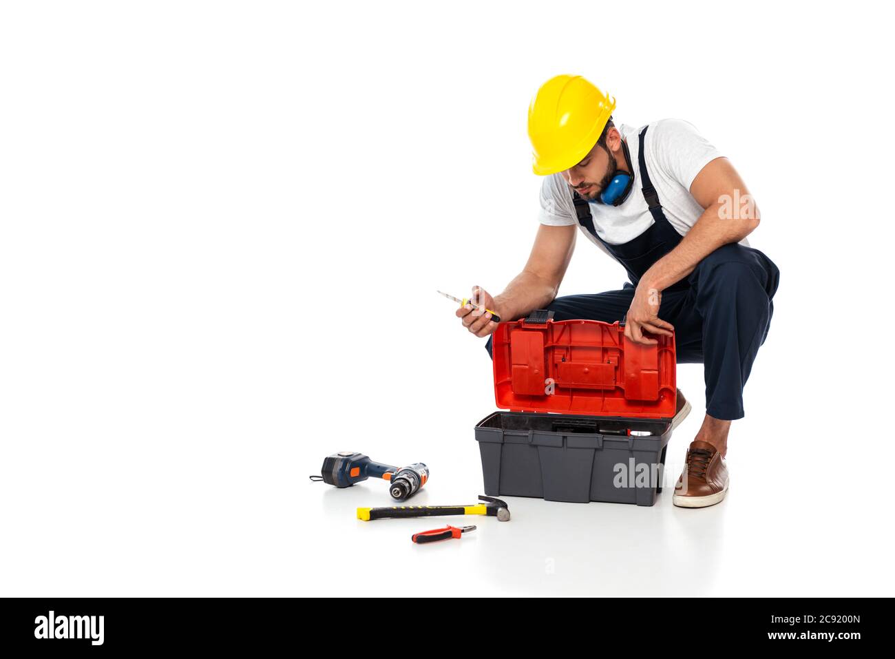 Workman in hardhat and ear defenders holding screwdriver near tools and ...