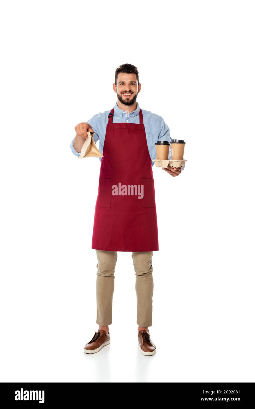 Handsome positive waiter holding paper bag and disposable cups on white ...