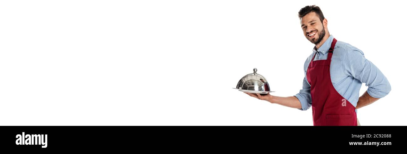 Panoramic crop of smiling waiter looking at camera while holding tray ...
