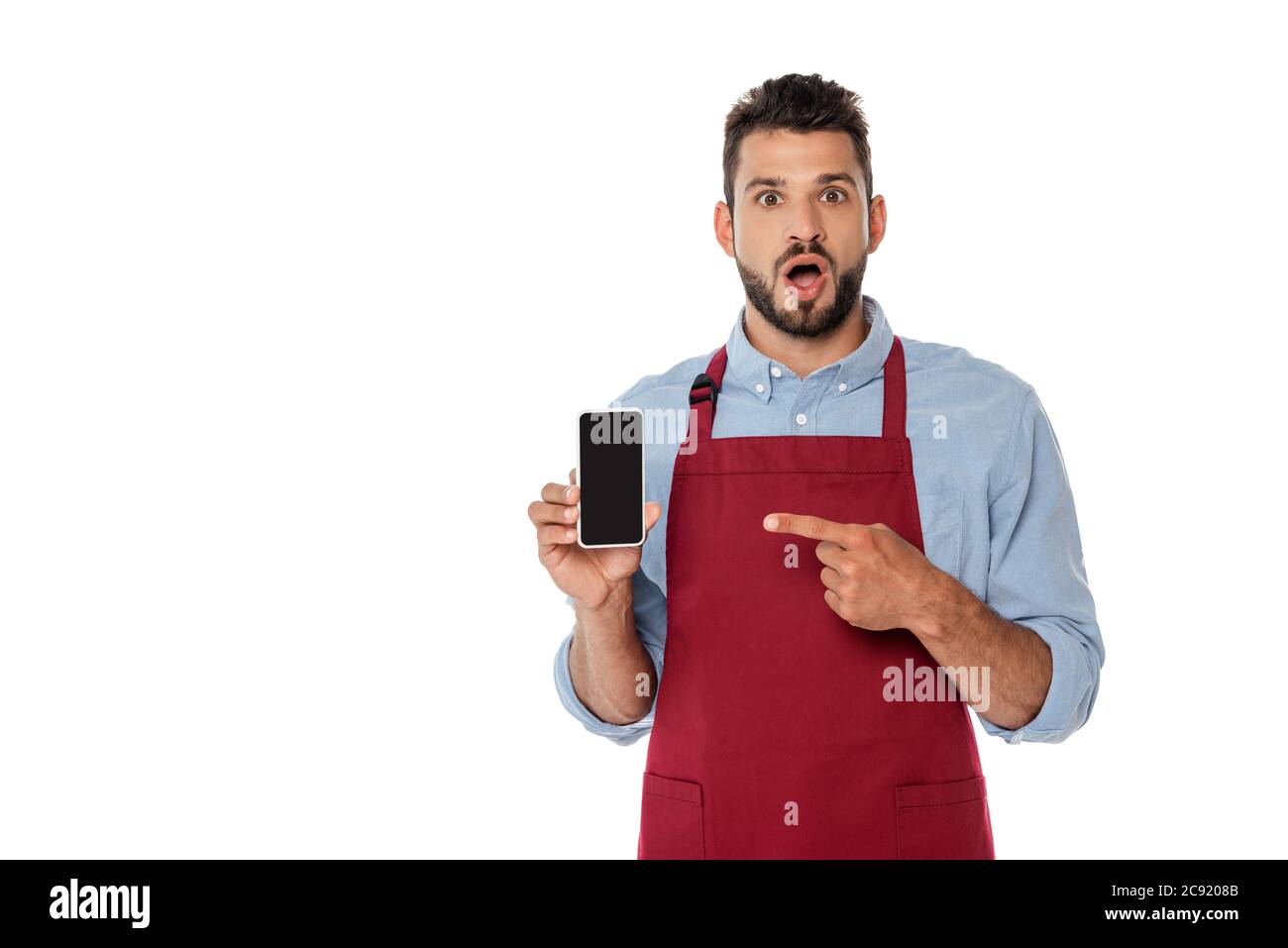 Surprised waiter in apron pointing with finger at smartphone with blank ...