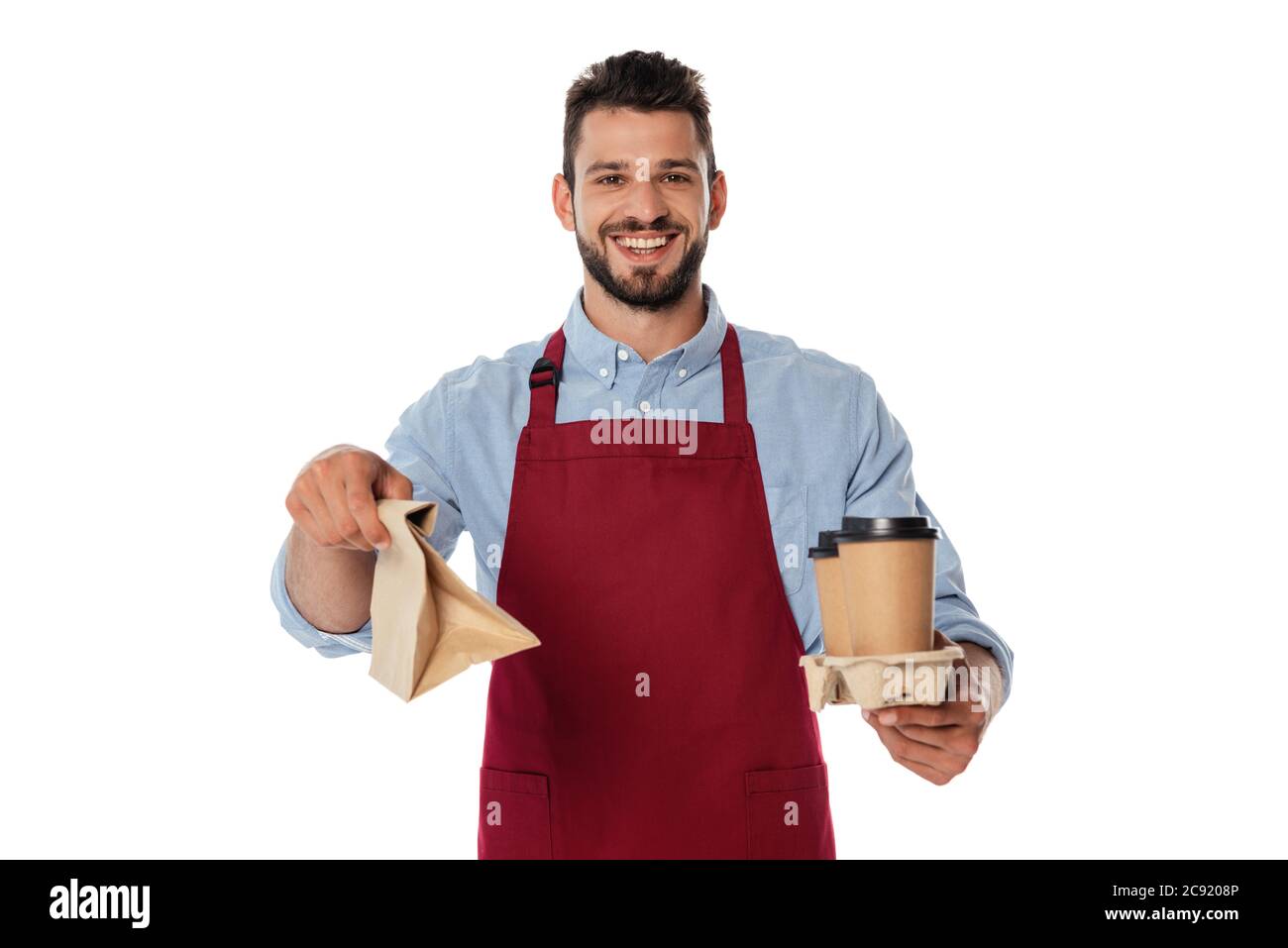 Positive waiter holding coffee to go and paper bag while looking at ...