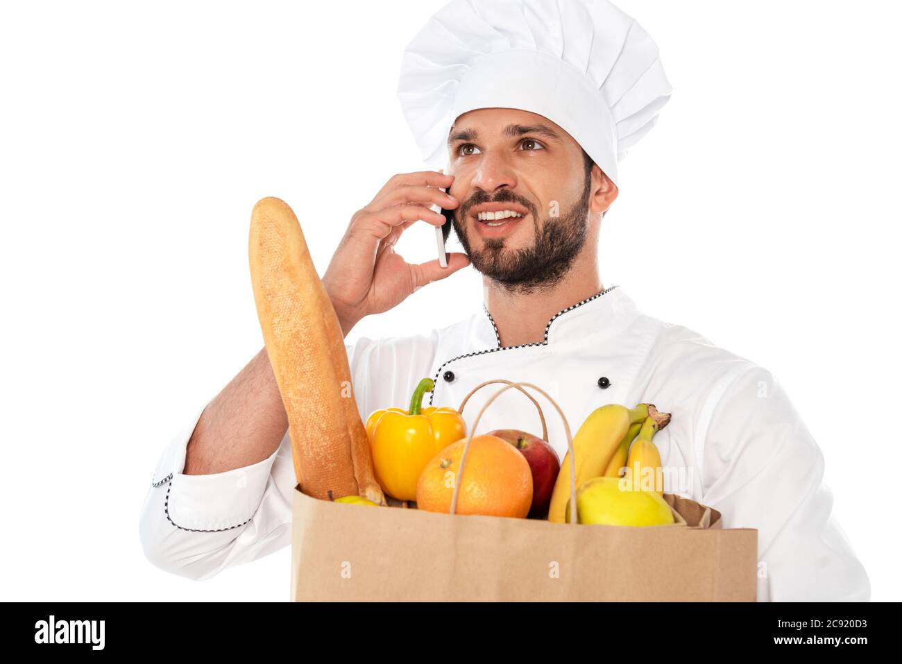 Smiling cook talking on smartphone and holding shopping bag with food ...