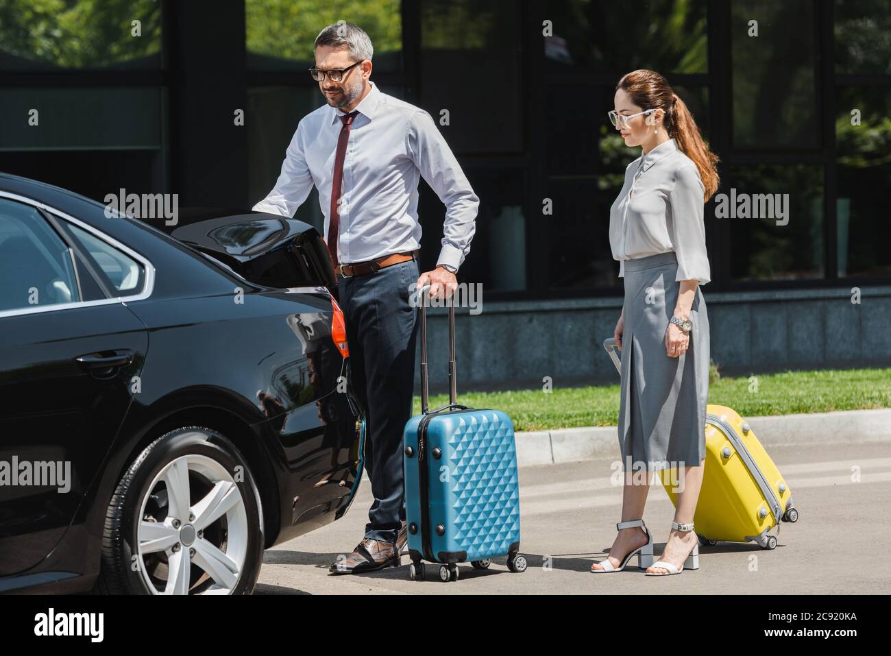 Businessman opening car trunk near businesswoman and baggage on urban ...