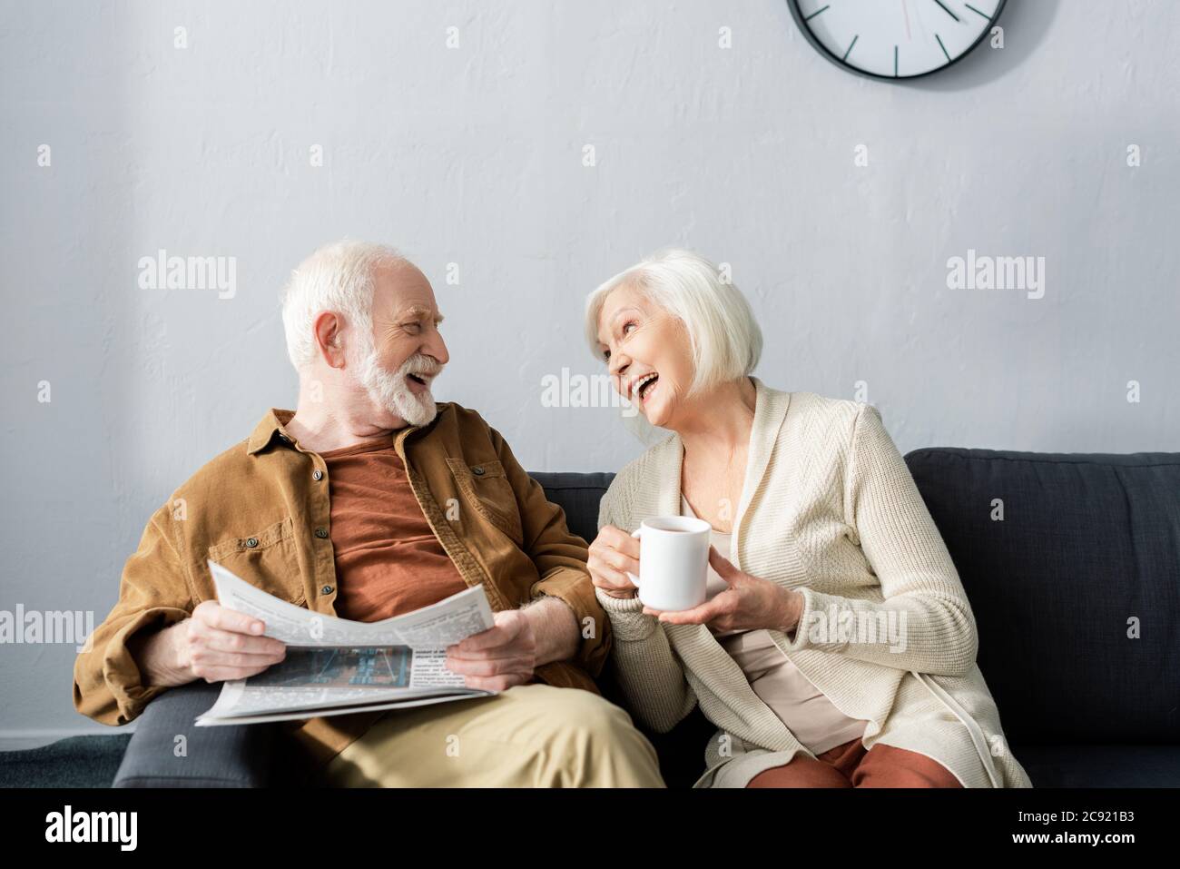happy senior couple talking while sitting on sofa at home Stock Photo ...