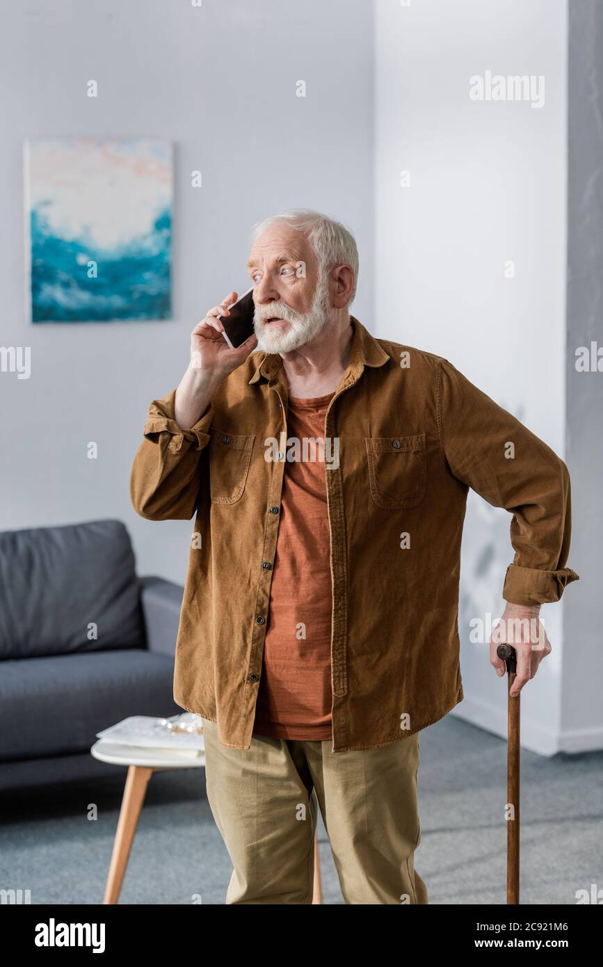 shocked senior man talking on smartphone while standing with walking ...