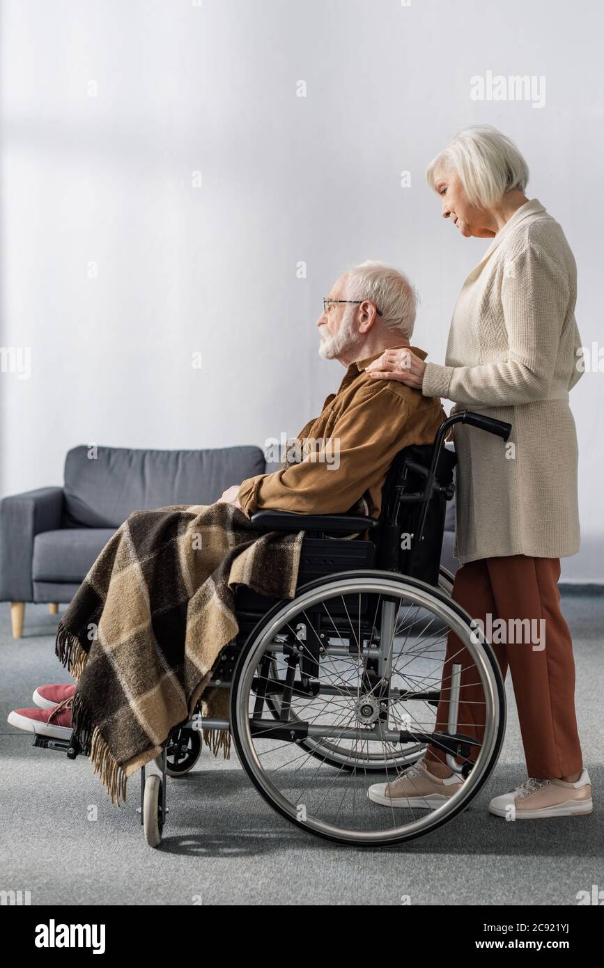 side view of senior woman touching shoulder of handicapped husband ...