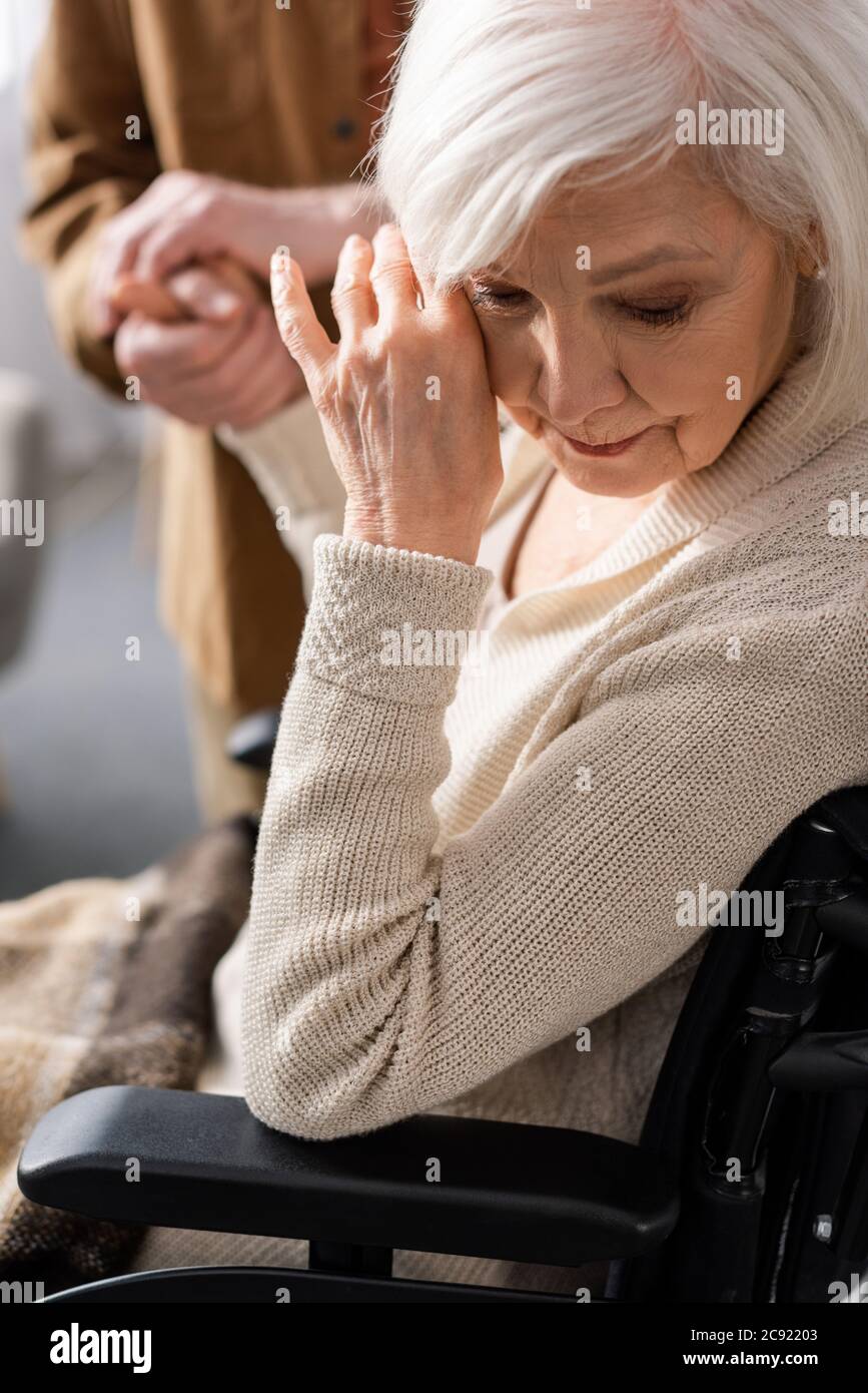 cropped view of man holding hand of disabled wife, sick on dementia ...