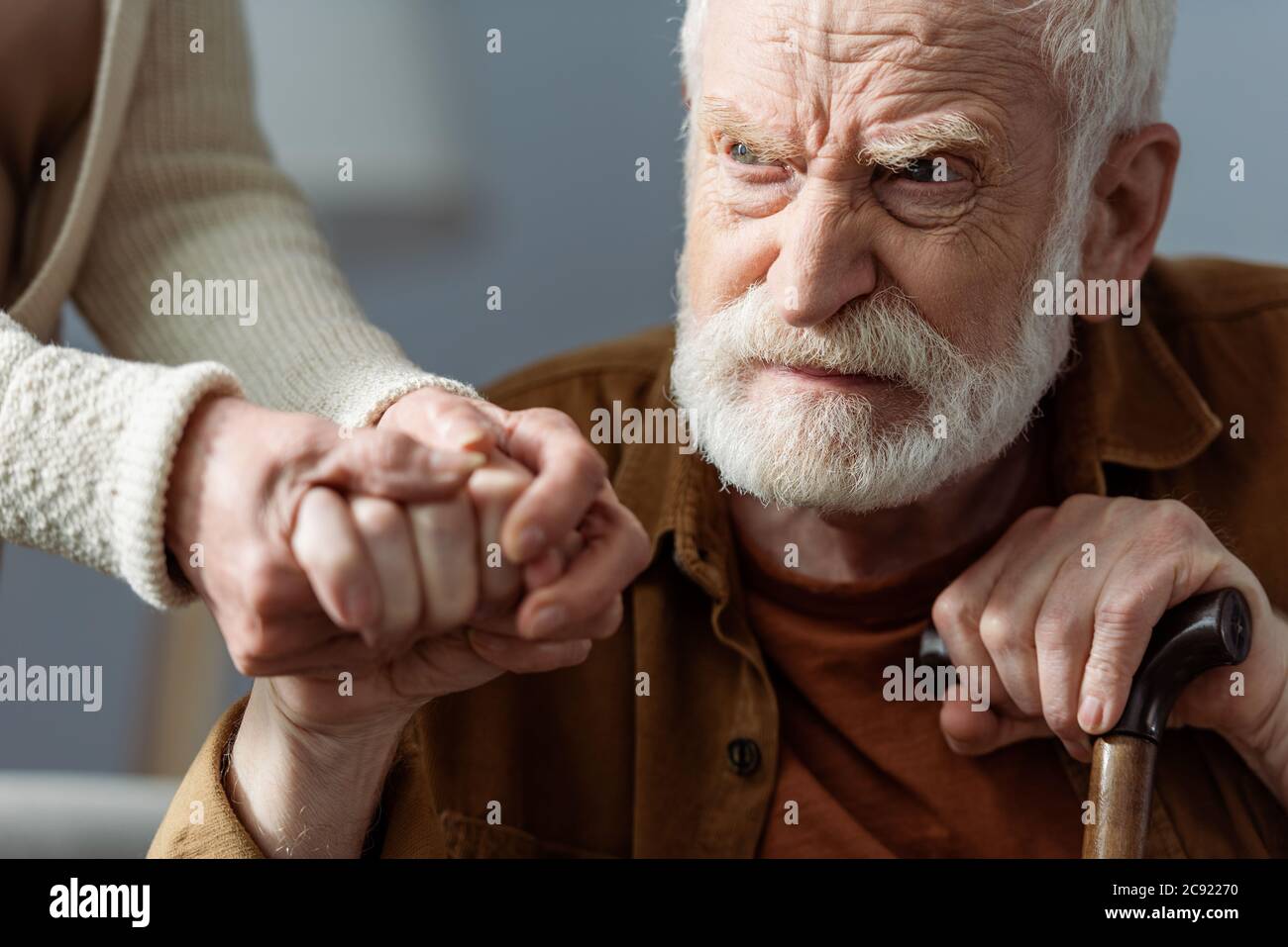 partial view of woman holding hand of senior husband, sick on dementia ...