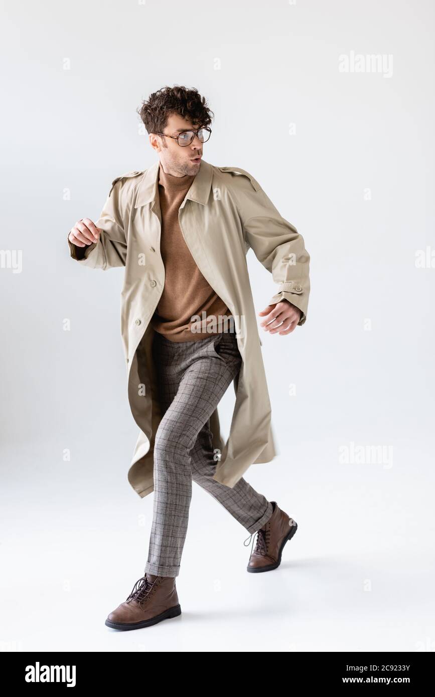 trendy, frightened man running and looking back isolated on grey Stock ...