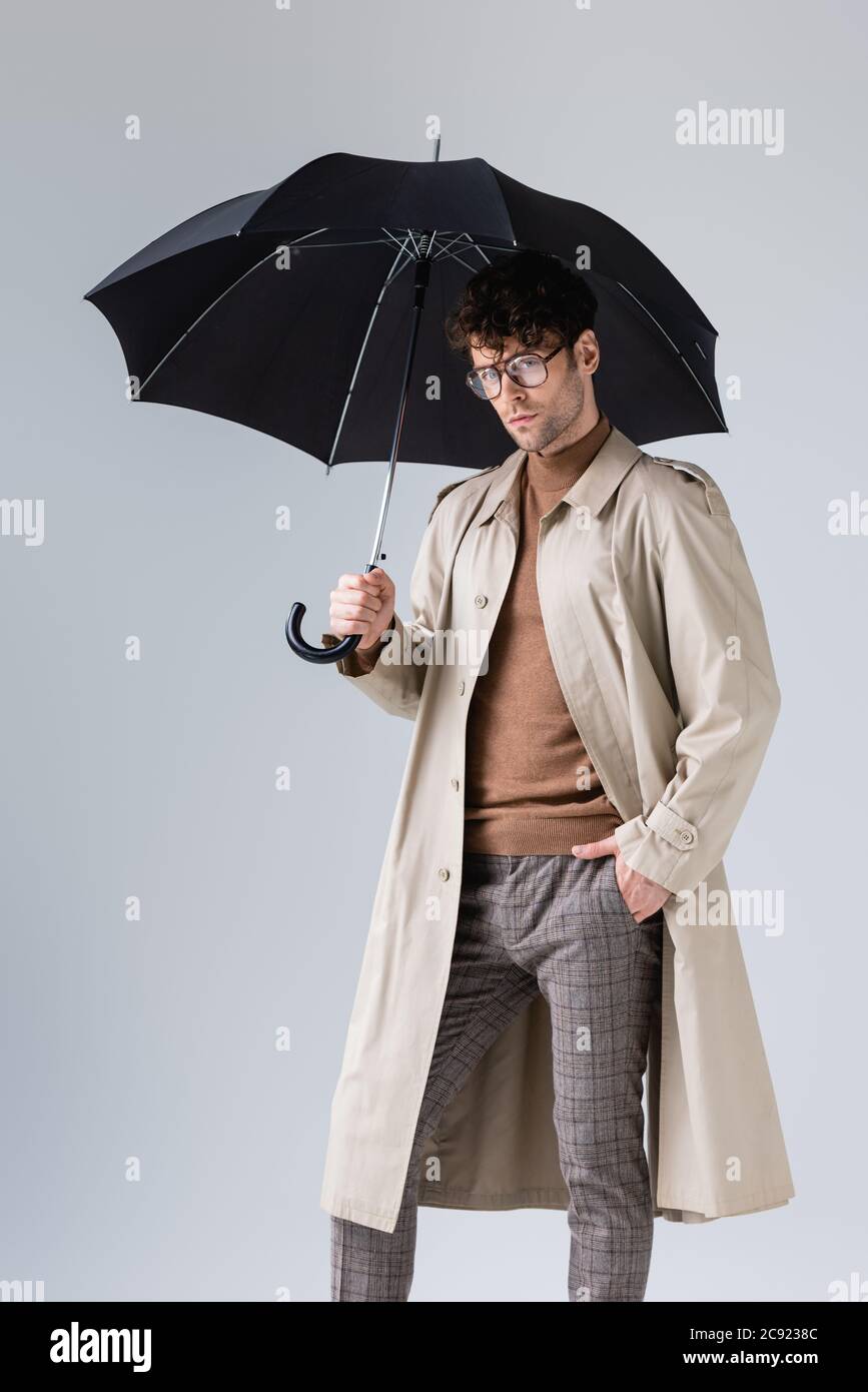 confident, trendy man standing under umbrella with hand in pocket on ...