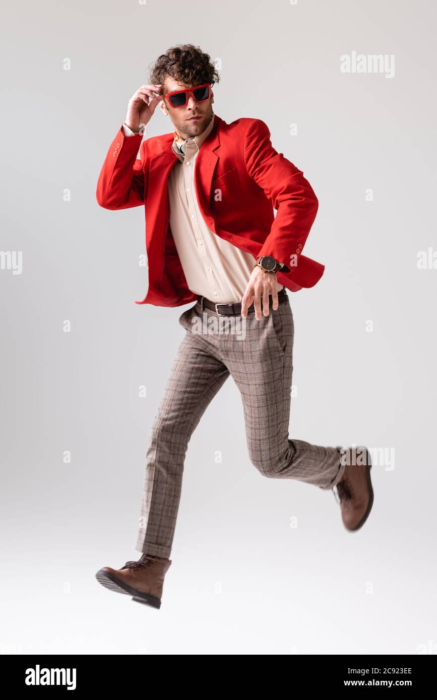 full length view of trendy man touching sunglasses and looking back ...